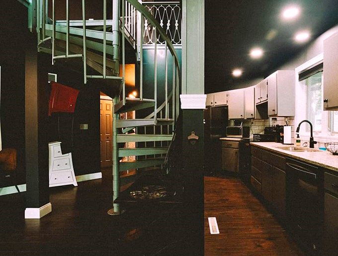 A spiral staircase winds upward like a metal serpent, connecting the kitchen to upper levels with industrial-gothic flair.