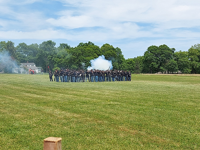 Civil War reenactors stand in formation, their muskets raised as smoke billows dramatically across the battlefield demonstration.