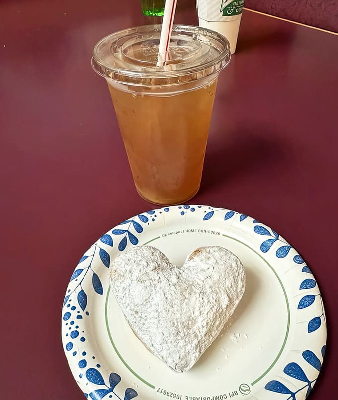 A heart-shaped beignet paired with green iced tea proves that not every great combination involves coffee, though the powdered sugar is non-negotiable.