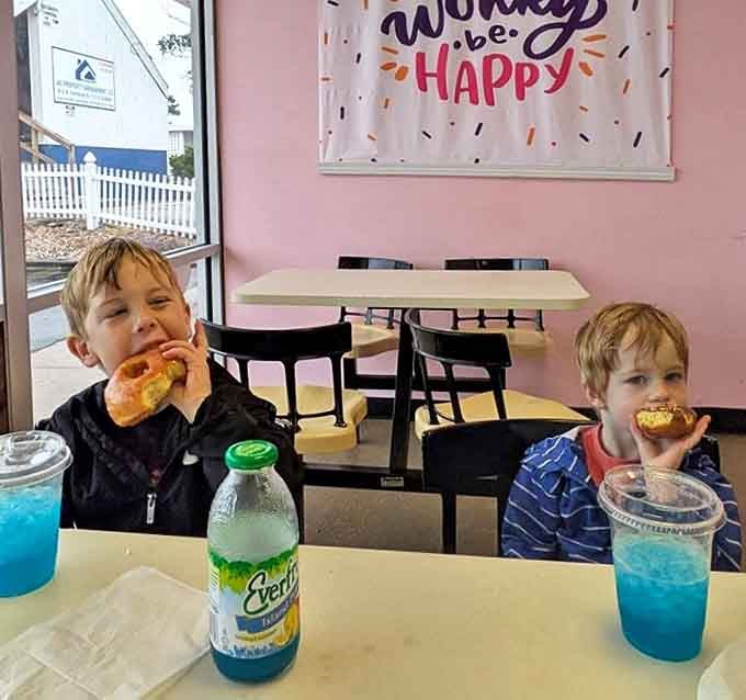 Two young connoisseurs engage in serious donut evaluation &ndash; the blue drinks suggest they've already mastered the art of complementary pairings.