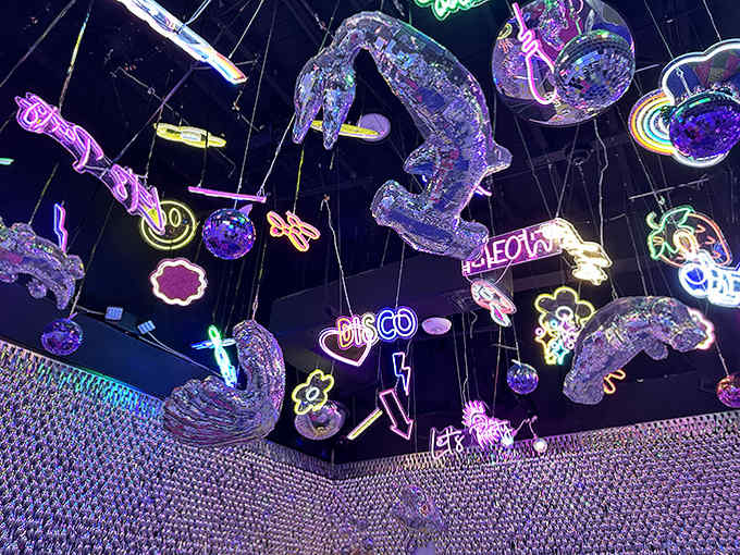 Look up at the disco celestial ceiling where neon signs and translucent figures float in a party that transcends dimensions.