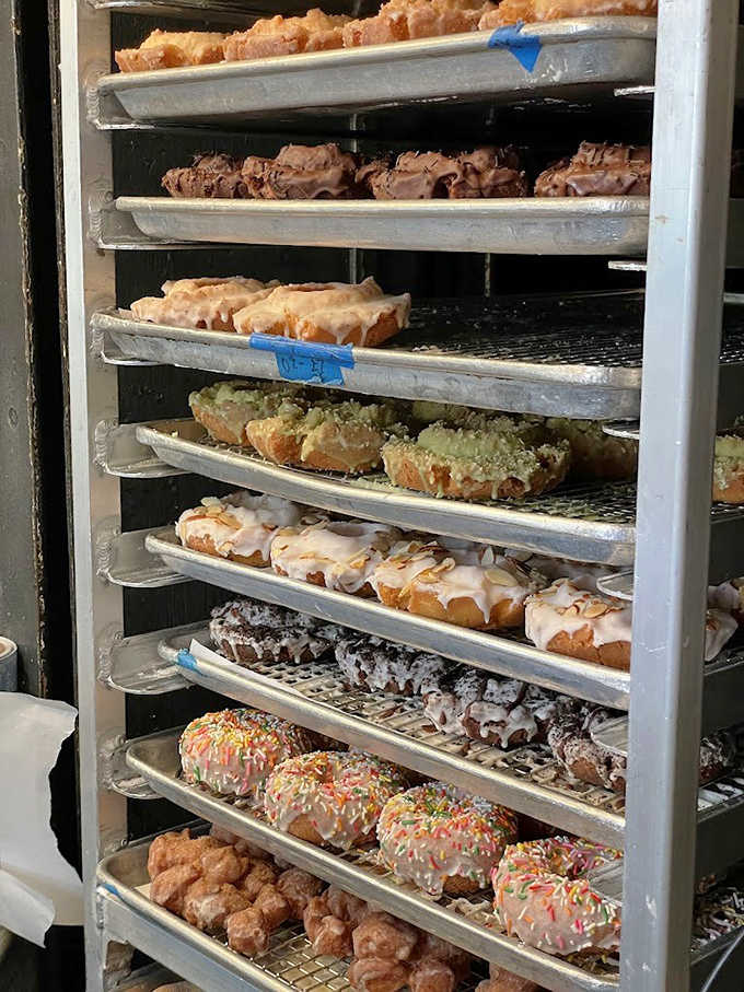 Fresh donuts cooling on the rack, a behind-the-scenes glimpse of edible art forms waiting to meet their destiny in white paper bags.