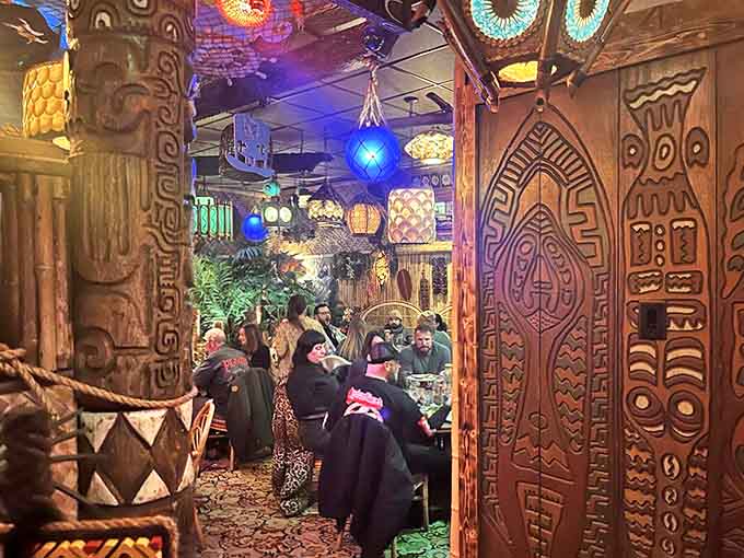 The dining area buzzes with energy as patrons enjoy their tropical escape. Carved wooden panels and colorful lighting transform an ordinary evening into an exotic adventure.