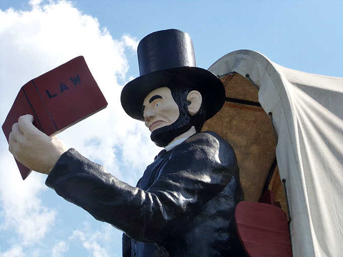 Lincoln looms cheerfully, law book raised, guarding the world’s largest covered wagon like history’s most polite roadside sentinel ever today.