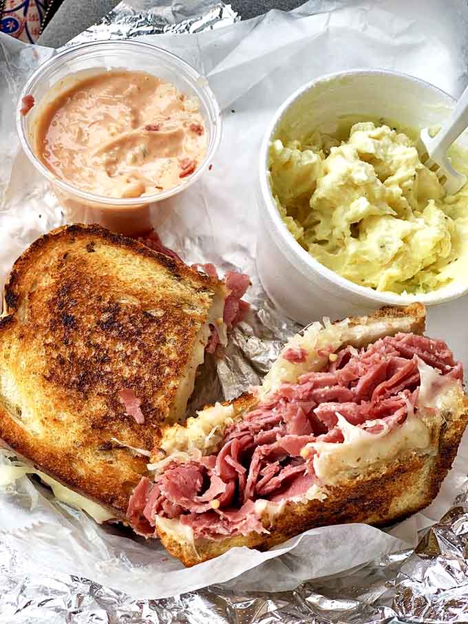 Reuben Sandwich with sides: The perfect trio&mdash;a classic Reuben flanked by creamy potato salad and tangy Thousand Island dressing.