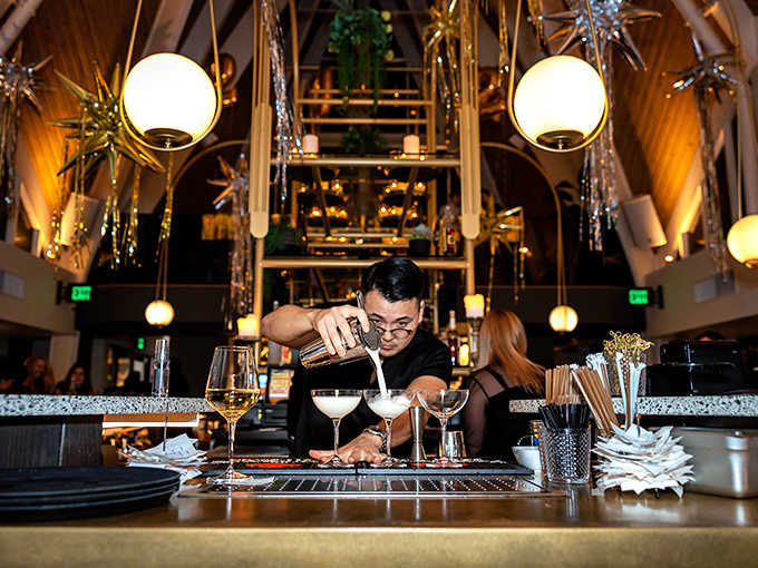 Mixologists work their magic beneath the dramatic vaulted ceiling, creating cocktails that complement the Mediterranean menu with theatrical flair.