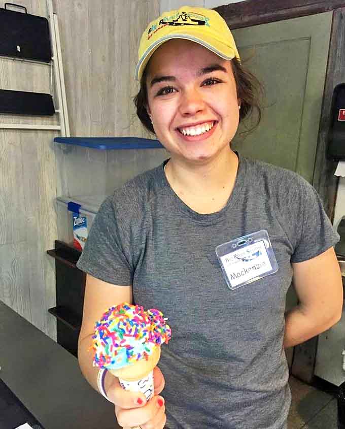 A friendly staff member showcases a rainbow-sprinkled creation, embodying the joy that comes with serving happiness by the scoop.
