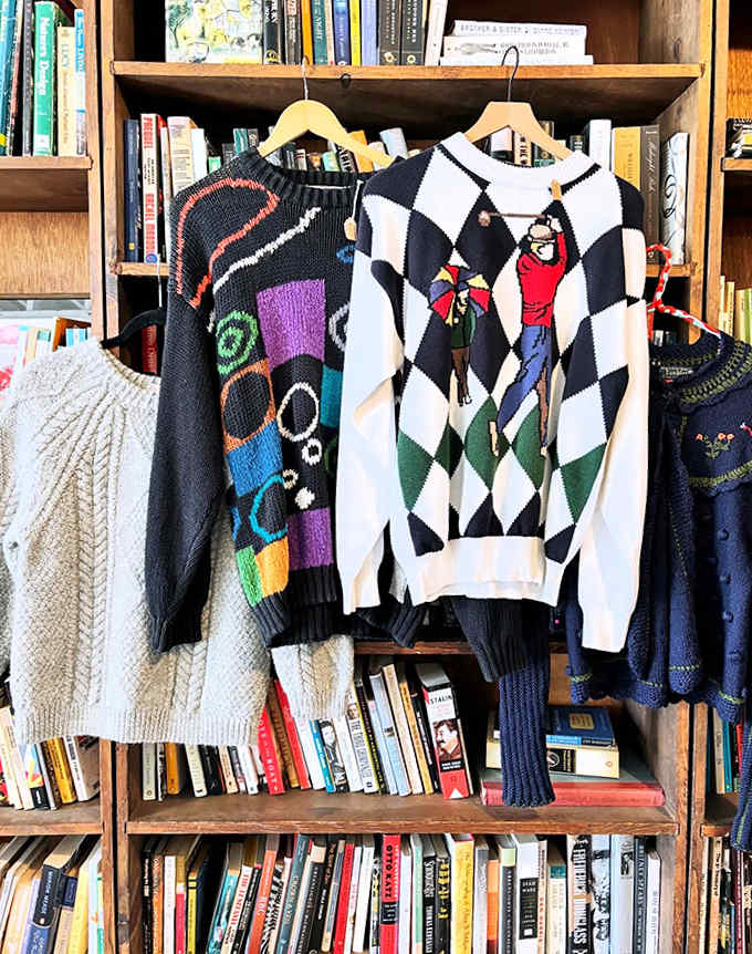 Knitted time capsules from the 1980s and 90s hang like textile art against a backdrop of literary classics.