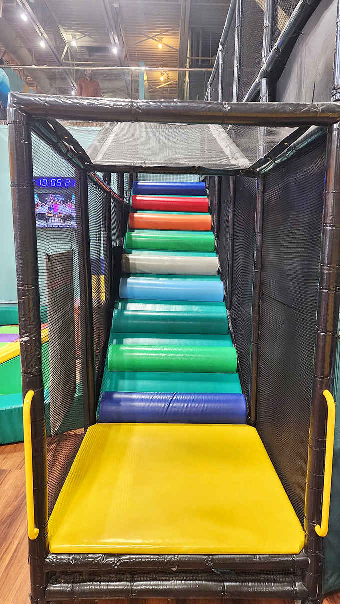 A rainbow-hued stairway of rolling cylinders creates a challenging path upward, like climbing a waterfall made of colorful, slightly wobbly stepping stones.