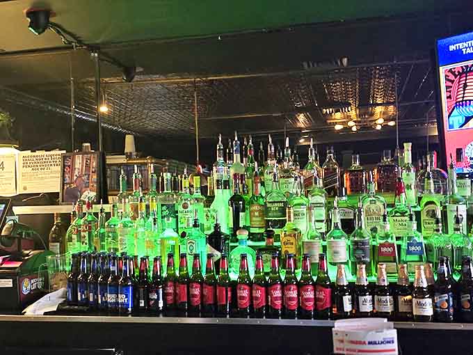 The well-stocked bar glows with that signature green light, bottles gleaming like treasures waiting to complement your pizza adventure.