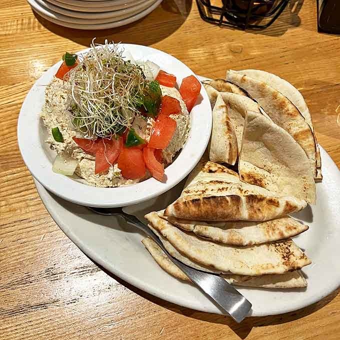 Hummus Dip: Velvety hummus topped with fresh tomatoes and sprouts, surrounded by warm pita triangles &ndash; the perfect starter to share (or not).