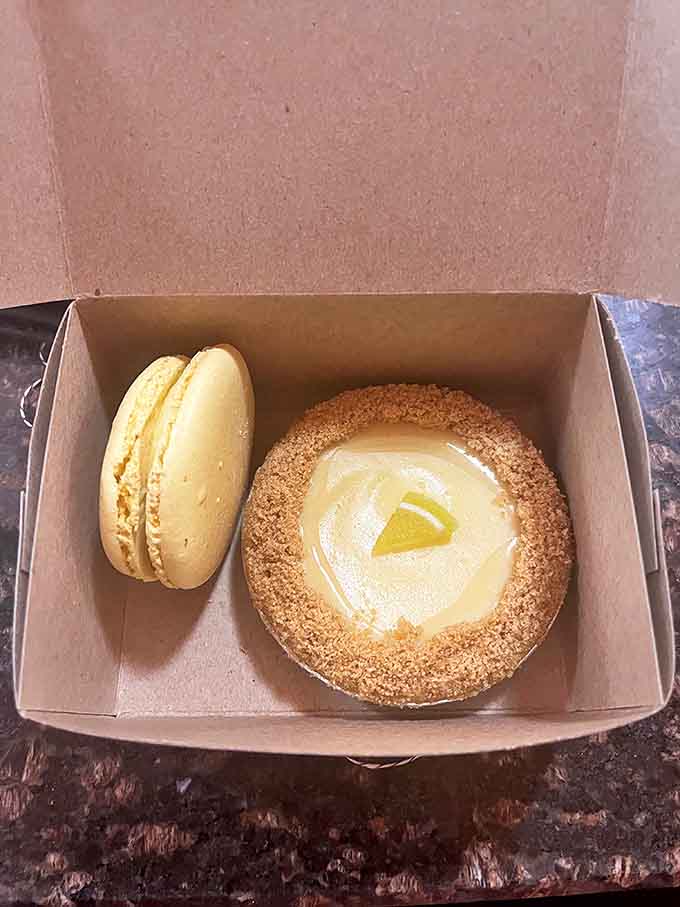 A study in contrasts: delicate macaron shell meets creamy filling, while a tart's buttery crust cradles lemon custard topped with a sunny citrus slice.