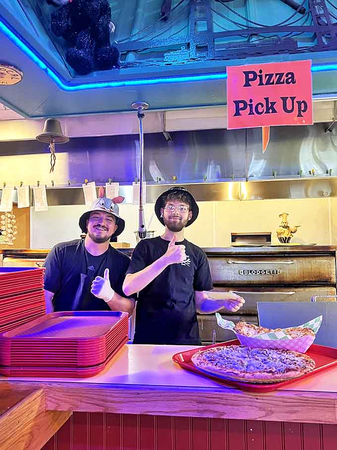 The enthusiastic pizza team gives thumbs up, ready to serve up slices that satisfy both hunger and curiosity in this unique establishment.