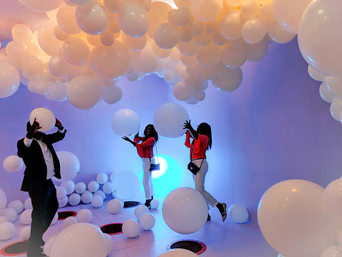 The white balloon room transforms visitors into weightless explorers, wading through a cloud-like sea illuminated by changing colored lights.