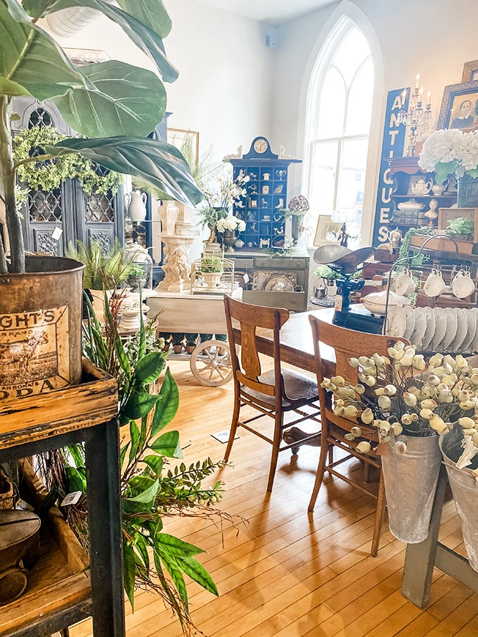 Sunlight dances through arched windows in this heavenly space where vintage furniture, greenery, and architectural elements create a decorator's paradise.