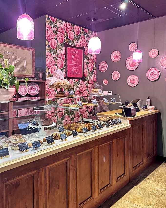 Pink floral wallpaper, vintage plates, and wooden display cases create a space that feels like the stylish living room of your French grandmother.