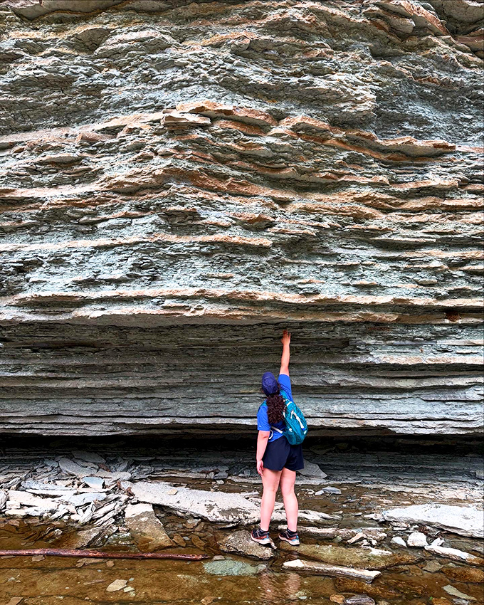 A hiker contemplates the massive rock formation, where each layer represents thousands of years in Earth's patient timeline.