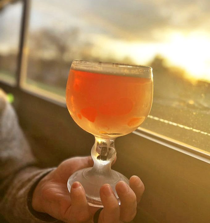 An 18-ounce schooner catches the sunset light, its contents glowing amber against the backdrop of Lake Michigan's evening sky.