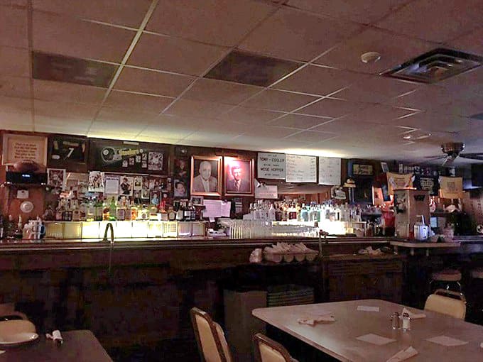 In the dim, amber glow of the bar, bottles gleam like promises while framed memories line the walls above.