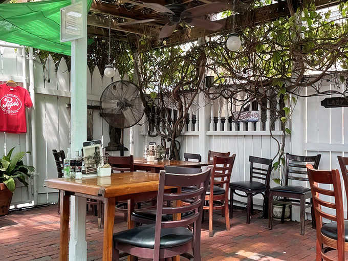 Covered Patio: Dappled sunlight filters through climbing vines in this garden-like sanctuary where ceiling fans stir the air and conversations flow as easily as the coffee.