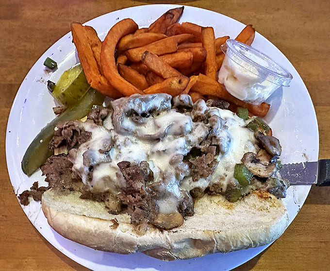 The Philly cheesesteak arrives overflowing with tender beef, melted cheese, and grilled peppers alongside perfectly crisp sweet potato fries.