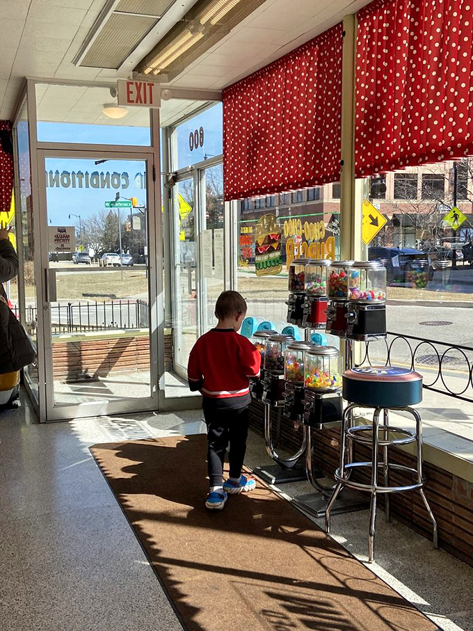 Gumball machines: Sunlight streams through the entrance, illuminating a young explorer contemplating the colorful treasures inside vintage candy dispensers.