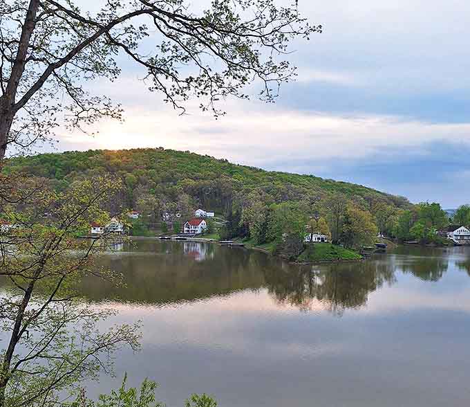 Morning mist creates a dreamy landscape where water meets sky, and lakeside homes peek through trees like a storybook village.