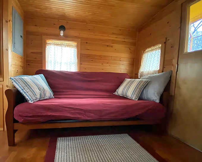 The burgundy couch adds a pop of color against the golden pine walls, creating a snug nook for afternoon naps or evening reading.