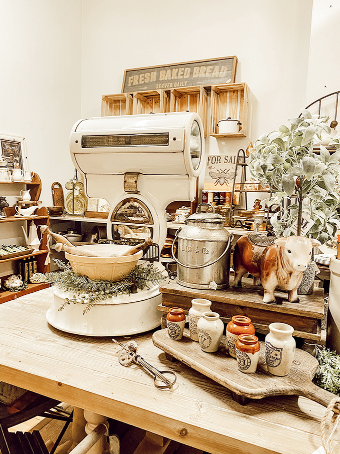 Farmhouse fresh! This rustic display featuring vintage bread boxes and ceramic cow creamers celebrates the timeless appeal of country kitchen collectibles.