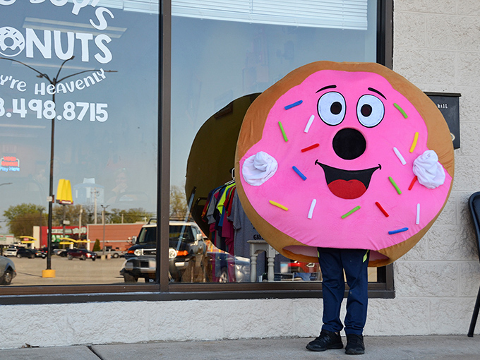 The donut mascot spreading joy outside – because nothing says "We take happiness seriously" like a giant smiling pastry.