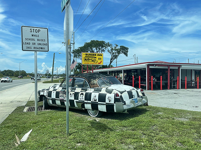 The classic drive-in exterior with its checkered car parked outside completes the time-travel experience that makes Burger Inn special.