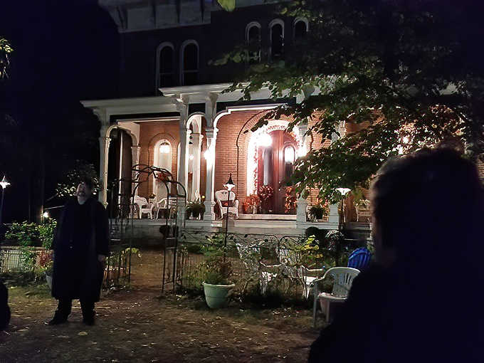 Shadowy figures approach the illuminated porch, perhaps unaware they're being watched by more than just the living residents.