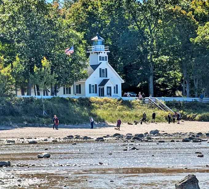 From the shoreline looking up, the lighthouse stands sentinel as it has for generations, while beachcombers explore the rocky shore.