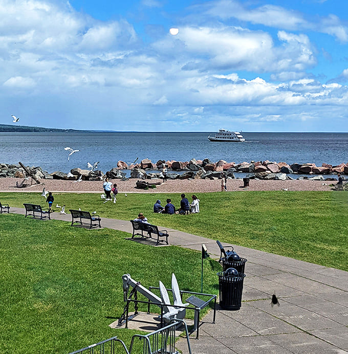 Visitors relax on the grass, proving that sometimes the best entertainment isn't on a screen but right before your eyes in the form of dancing waves and passing ships.
