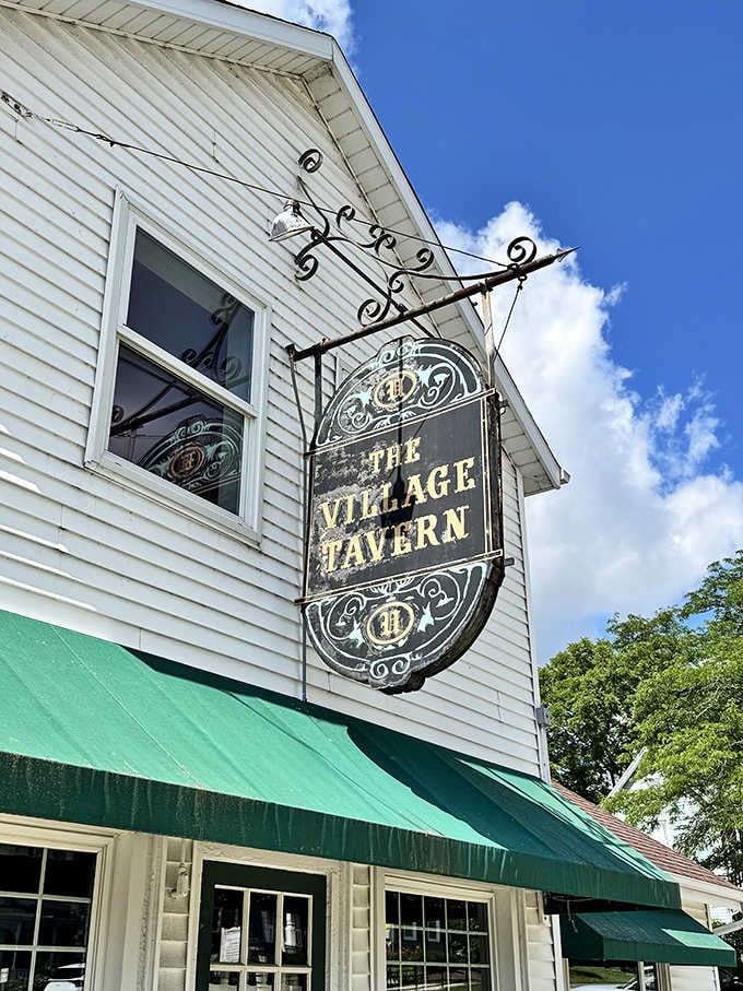 The Village Tavern's vintage sign swings gently in the breeze, a beacon for hungry travelers and locals alike seeking comfort food perfection.