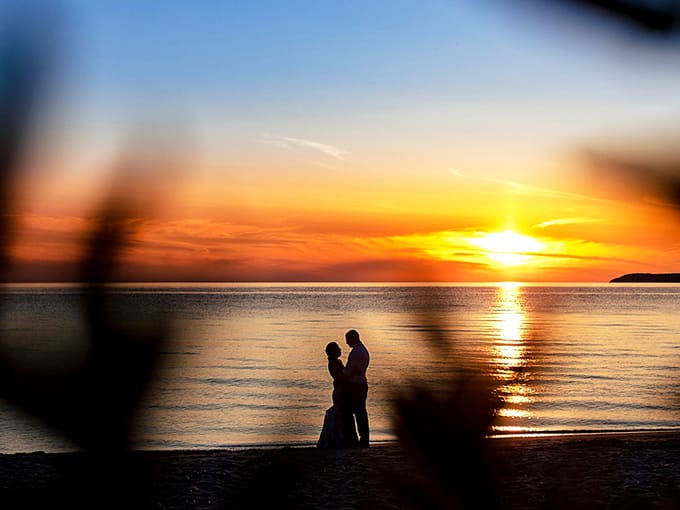 Two silhouettes against a fiery sunset remind us why Michigan's shores have witnessed countless proposals, anniversaries, and "I'm sorry" moments.