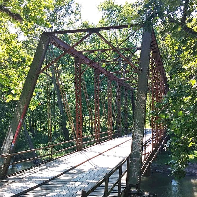 Summer foliage creates a green tunnel approaching the bridge, a natural gateway to this historic crossing.