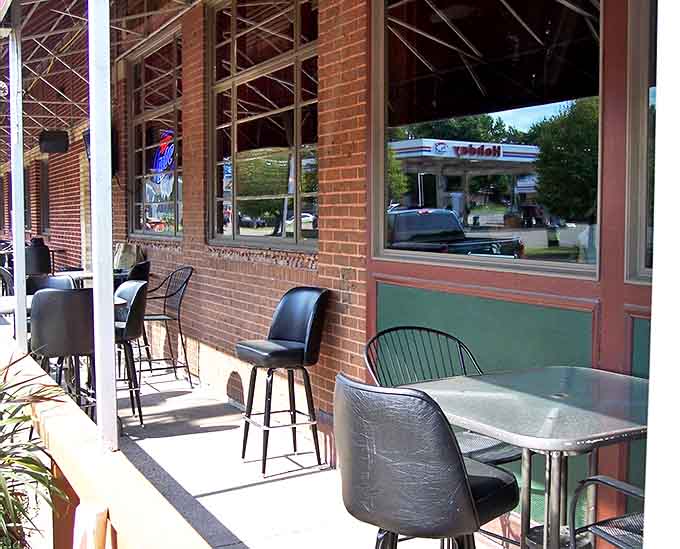 The outdoor seating area offers front-row views to Bayport life, where summer evenings stretch long and conversations flow as freely as the Minnesota breeze.