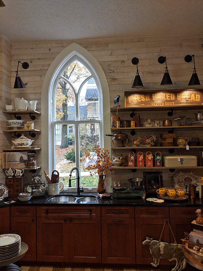 Cathedral windows frame this kitchen vignette perfectly, where open shelving showcases vintage treasures against warm wood and rustic elements.