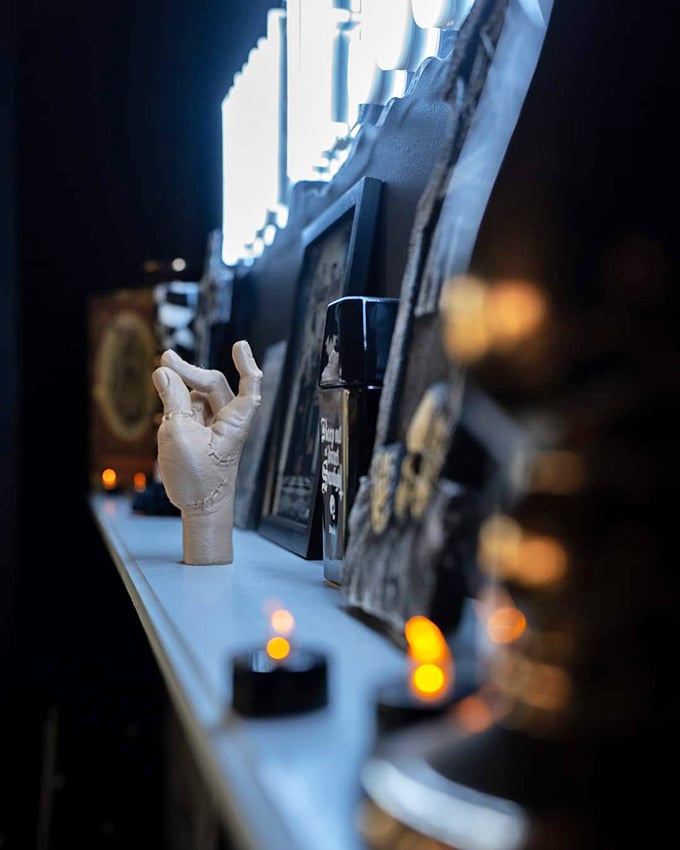Candlelight casts dramatic shadows across carefully curated shelves, where decorative hands reach out from the darkness.