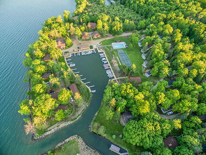 The resort reveals its perfect peninsula positioning in this aerial view, where cabins nestle among trees and boats find safe harbor.