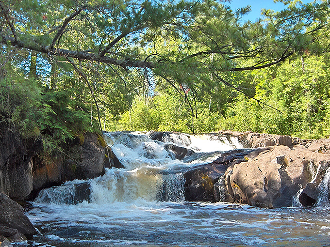 Sunlight dances through the trees at Breakwater Falls, where the rushing water has carved smooth channels through bedrock over thousands of years.