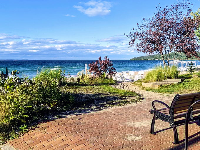 A brick pathway leads to Lake Street Beach's pristine shoreline, where blue waters meet golden sand under Michigan's vast sky.