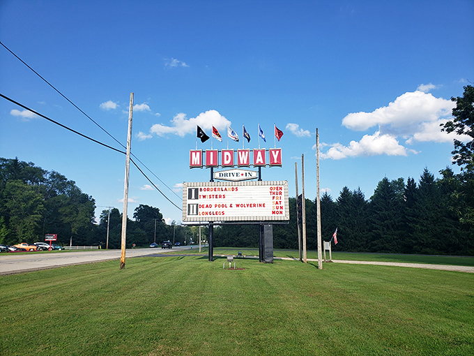 The iconic Midway Drive-In sign stands tall against blue skies, announcing today's double feature. Those colorful flags add a festive touch to this slice of Americana.