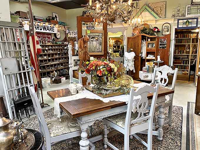 Step into a perfectly curated time capsule where elegant dining sets meet vintage hardware displays, all bathed in the warm glow of antique chandeliers.