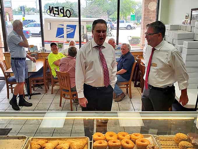 Morning regulars gather at wooden tables, trading neighborhood news while staff in crisp shirts orchestrate the daily donut ballet.