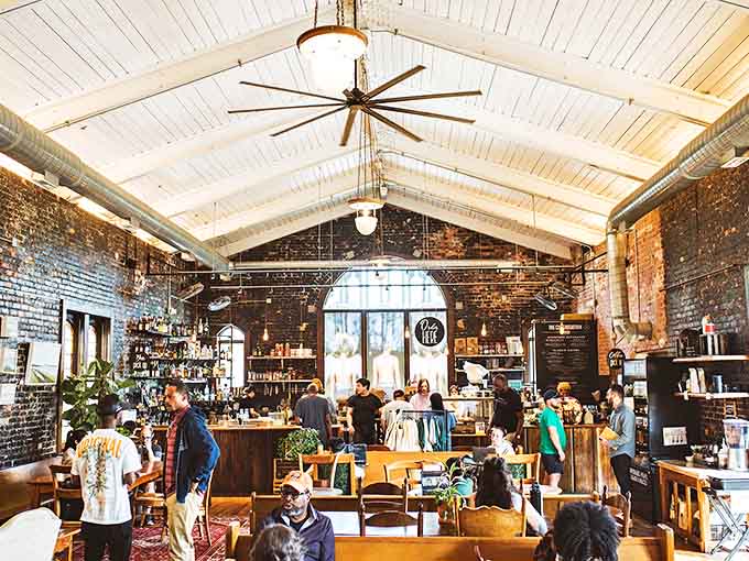 Exposed brick walls and soaring white ceilings create a reverent atmosphere where coffee devotees gather beneath industrial fans and warm lighting.