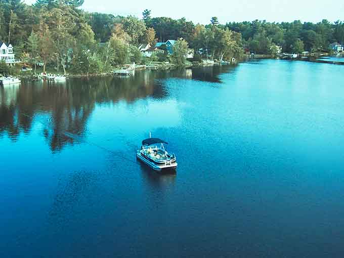 Tranquility defined: A lone pontoon drifts across crystal-clear waters, surrounded by the lush greenery that cradles Leelanau's hidden waterways.