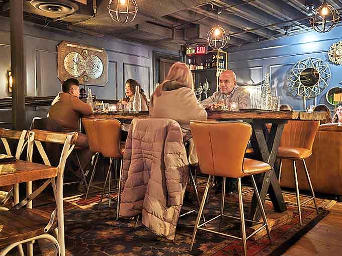 Plush leather chairs surround rustic wooden tables while globe pendant lights cast a warm glow over conversations that flow as smoothly as the spirits.