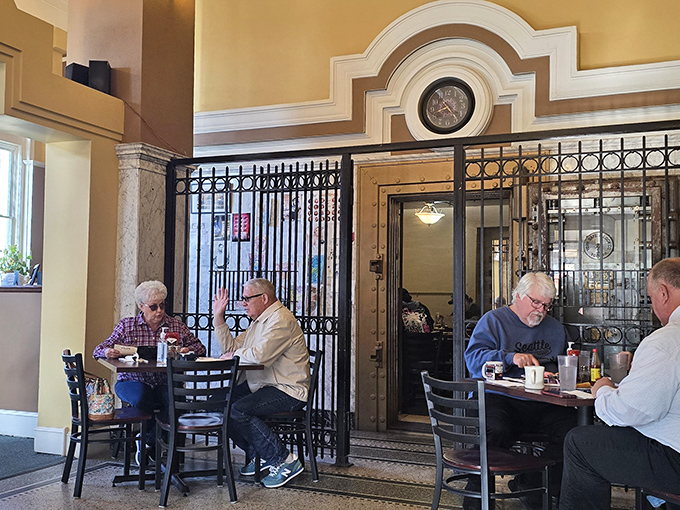 Inside, original wrought iron gates frame dining areas where bank tellers once counted cash and now servers deliver comfort food classics.